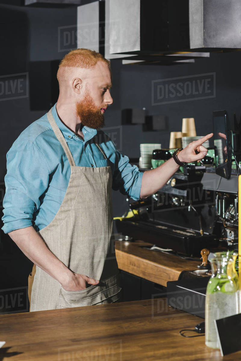 Side view of handsome young barista pointing at screen while working in ...