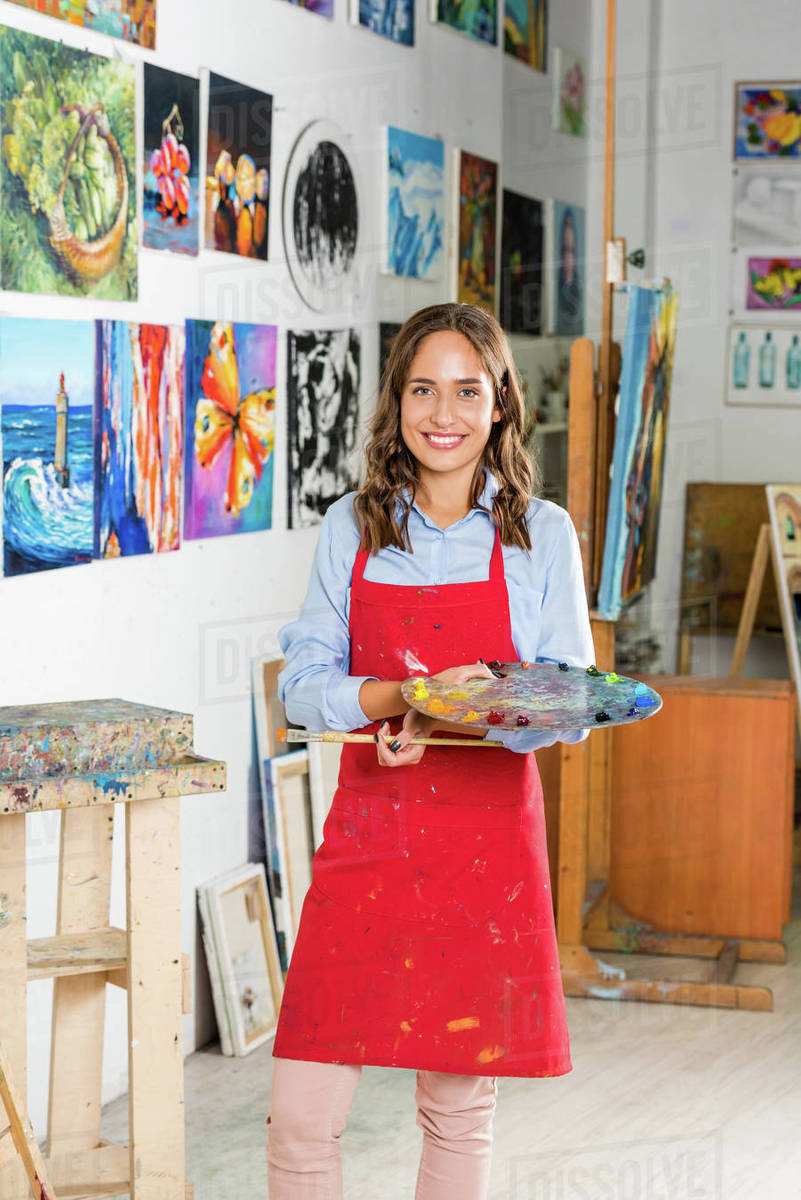 Beautiful female artist holding painting brush and palette in workshop ...