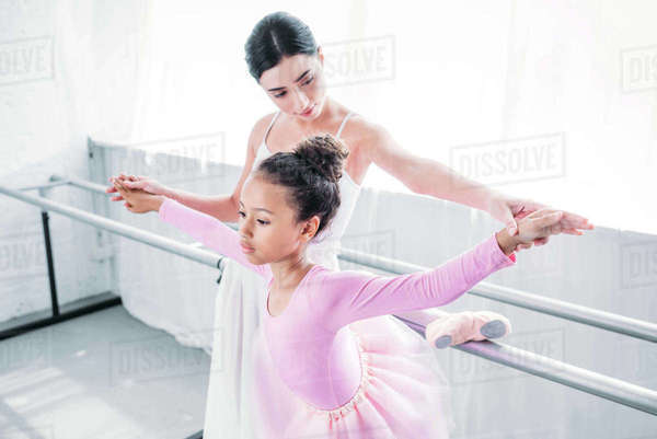 Cute african american child in pink tutu exercising with teacher in ...