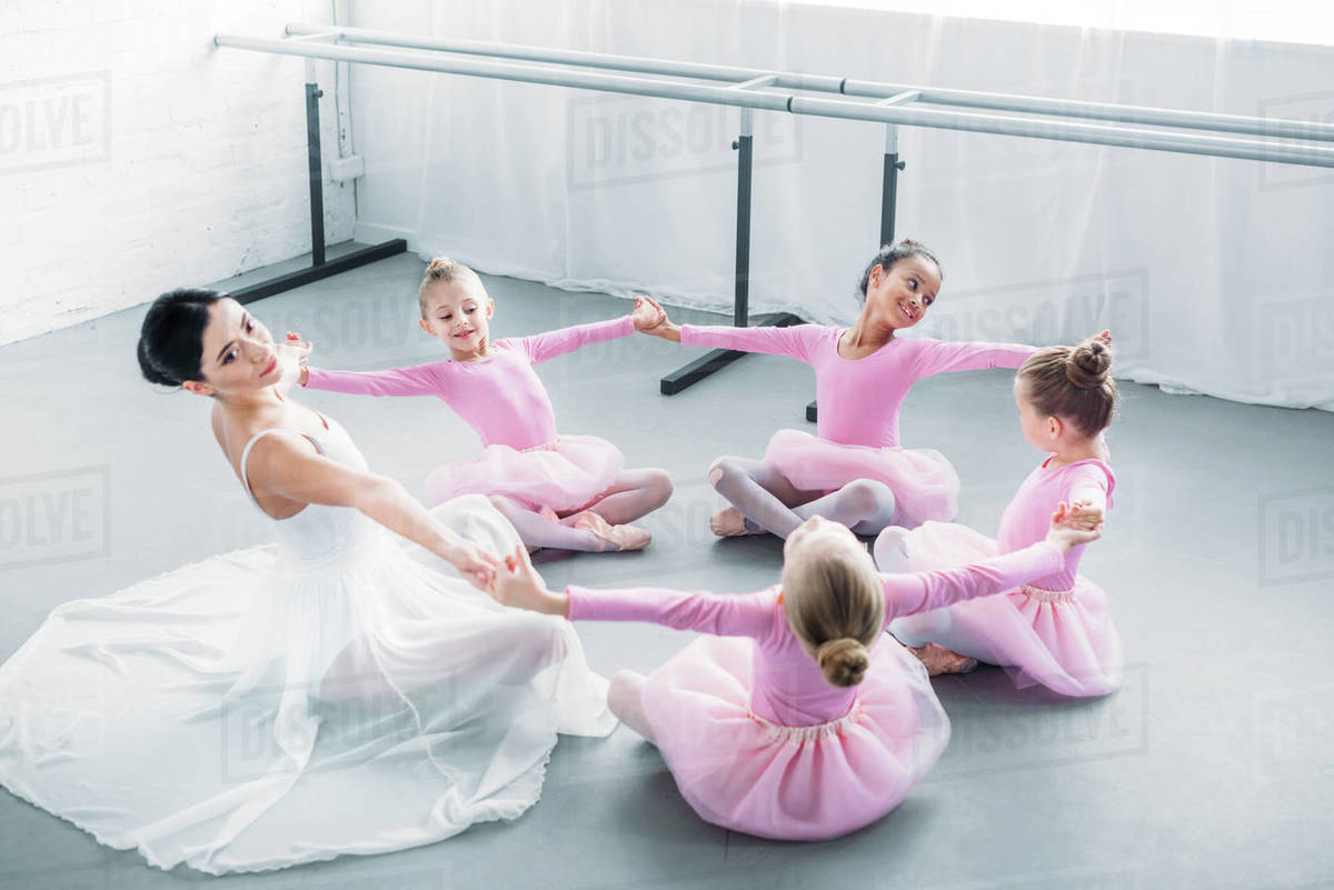 Adorable little ballerinas and young teacher practicing together in ...
