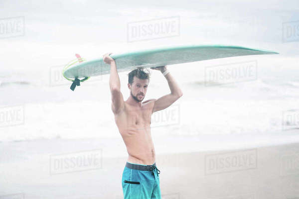 Surfer standing with surfboard on head and looking at camera in Bali ...