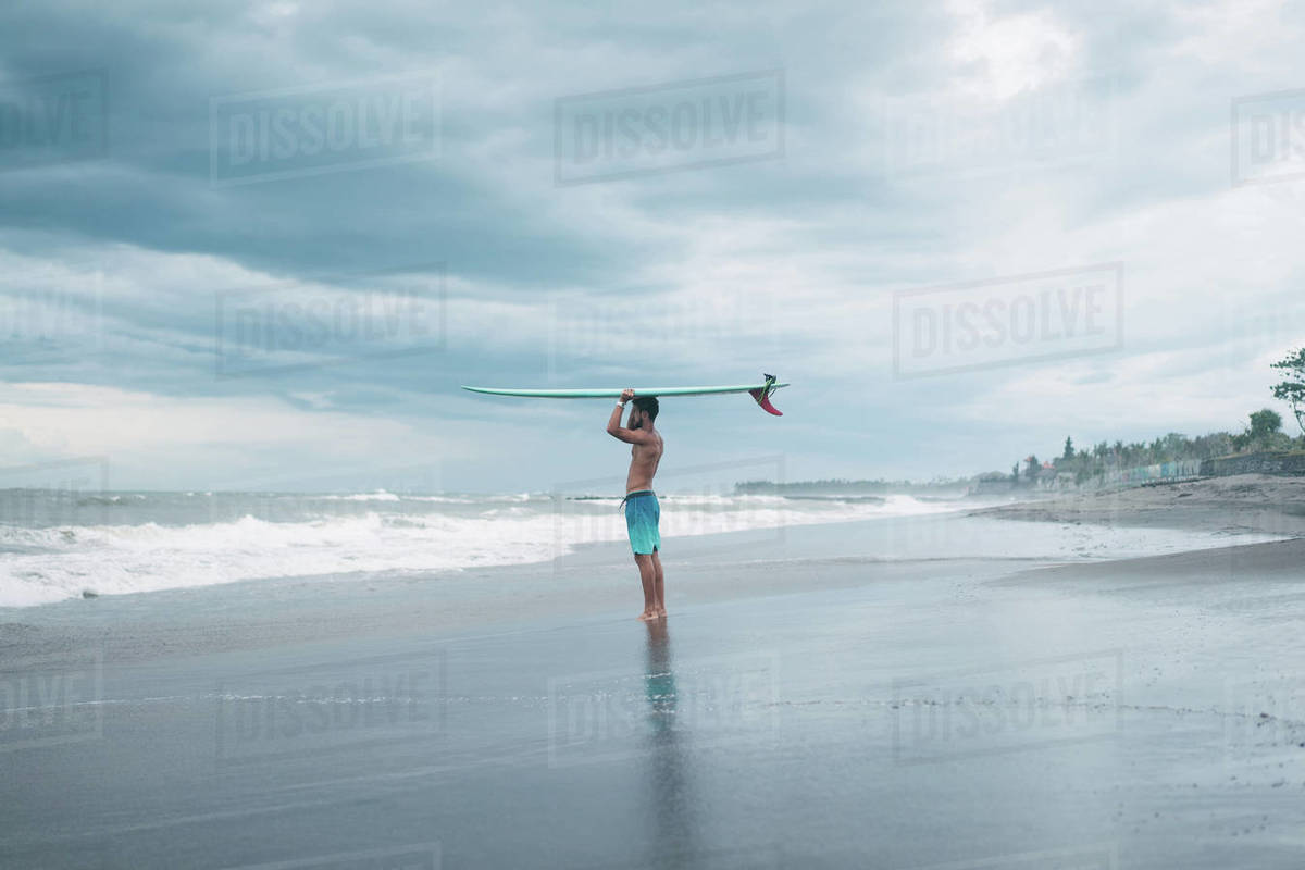 Surfer holding surfboard on head and looking at ocean in Bali ...