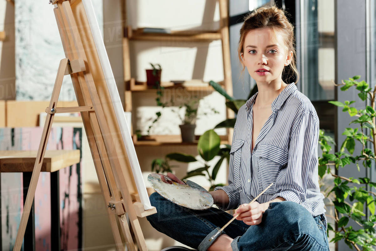 Attractive female artist sitting on bench and holding palette and ...