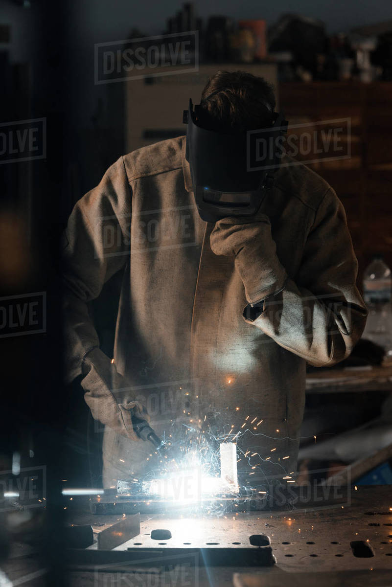Front view of welder in protection mask working with metal at factory ...