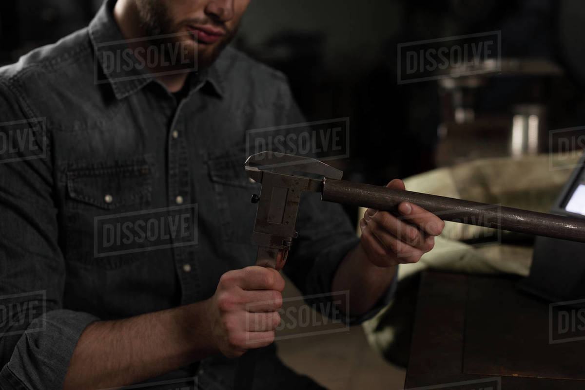 Cropped image of young workman measuring metal part at factory ...