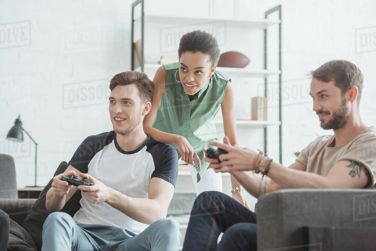 Young African american woman watching two men playing video game with ...