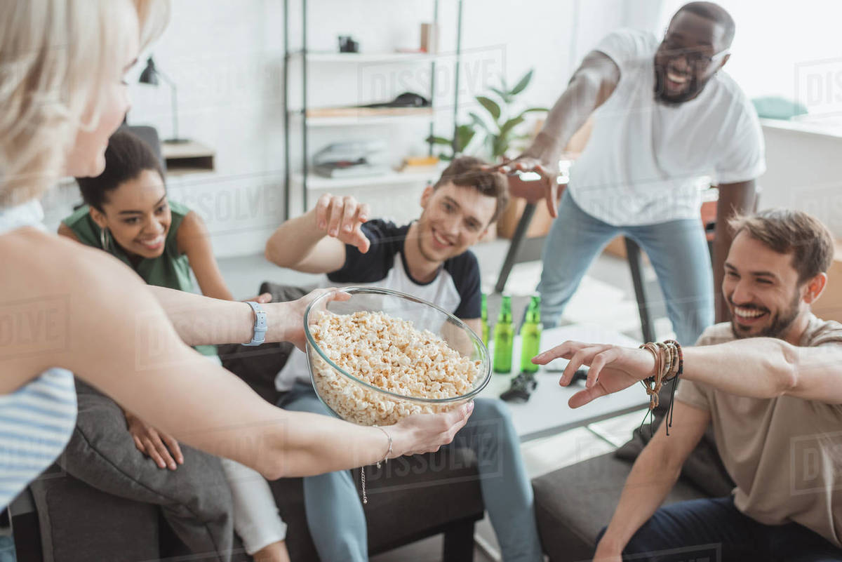 Cropped image of young woman giving bowl of popcorn to smiling ...