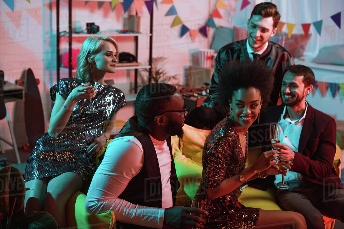 Multiracial smiling friends having party with drinks in decorated room ...