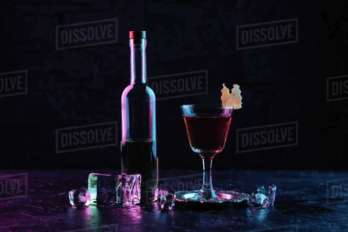 Glass of alcohol cocktail, bottle of liquor and ice cubes on dark ...