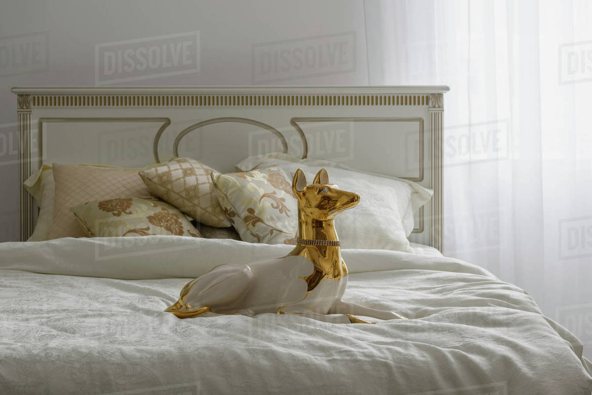 Dog statuette on bed with white linen in room - Stock Photo - Dissolve