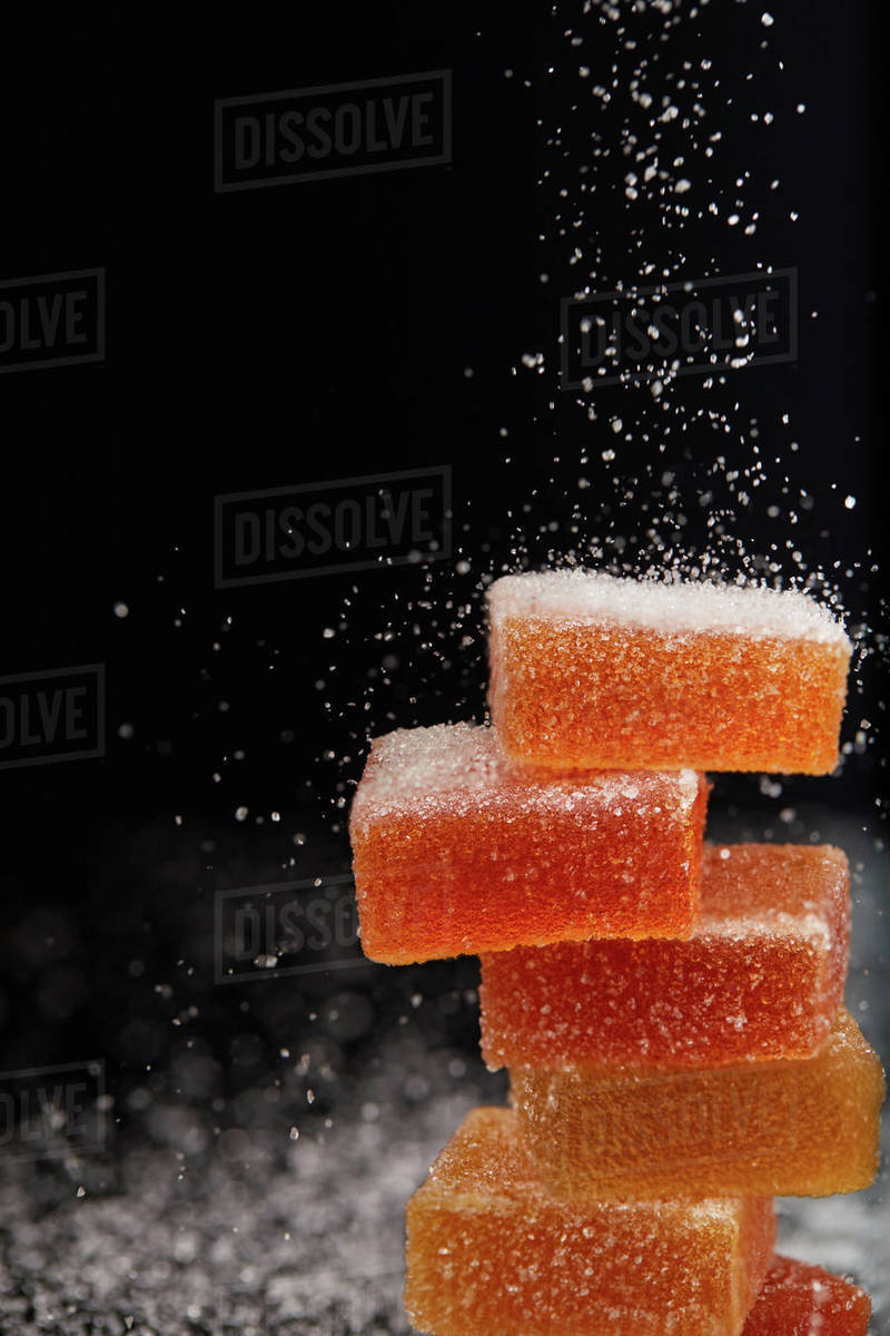 Close-up shot of sugar falling on jelly candies on black background ...