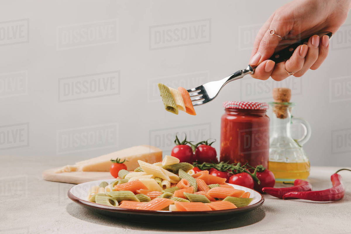 Cropped shot of woman eating colored pasta with fork on concrete ...