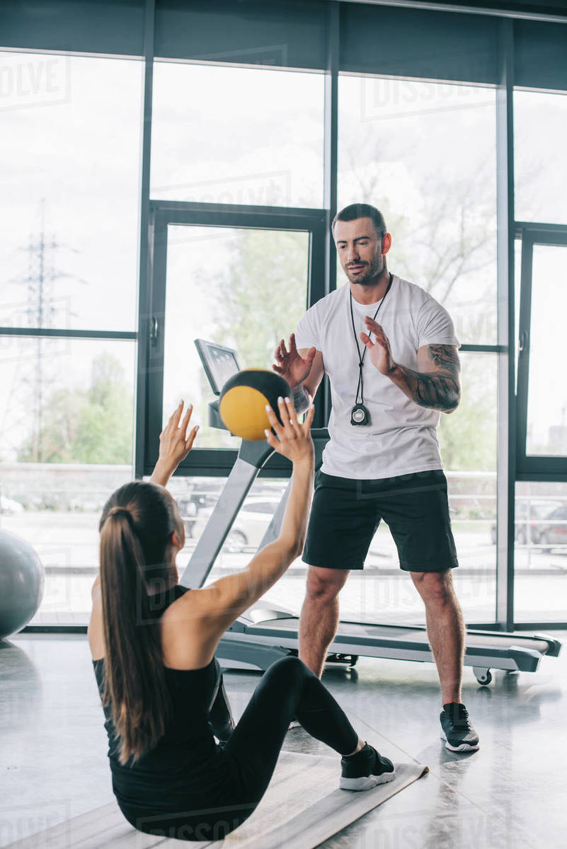 male personal trainer and sportswoman doing exercises with ball at gym ...