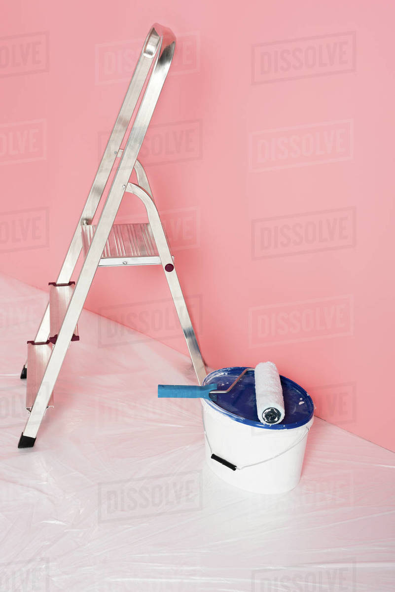 Close up view of paint roller on paint tin and ladder in front of ...