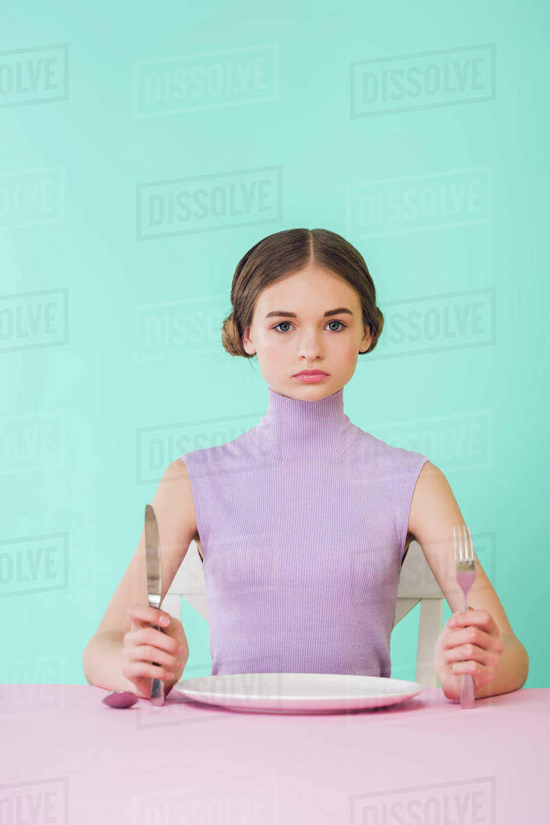 girl with knife, fork and empty plate sitting at table in dining room ...