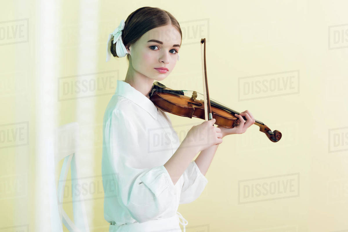 beautiful teenager in white outfit playing violin, isolated on yellow ...