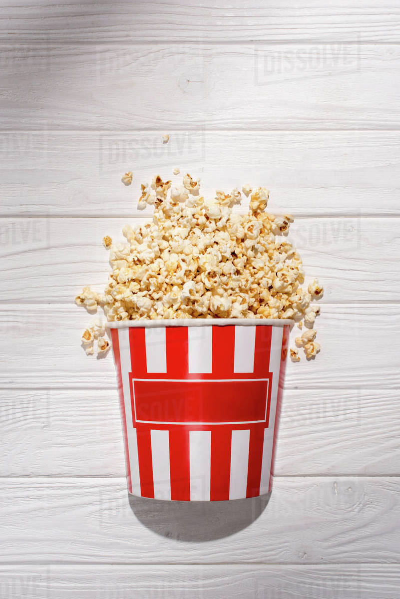 Flat lay with disposable bucket with popcorn on white wooden surface ...
