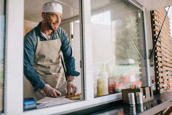 Handsome smiling young male chef looking away while cooking in food ...