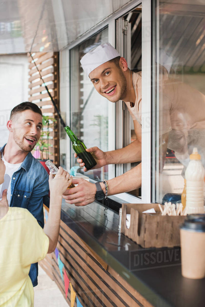 Smiling chef giving drinks to customers from food truck and looking at ...