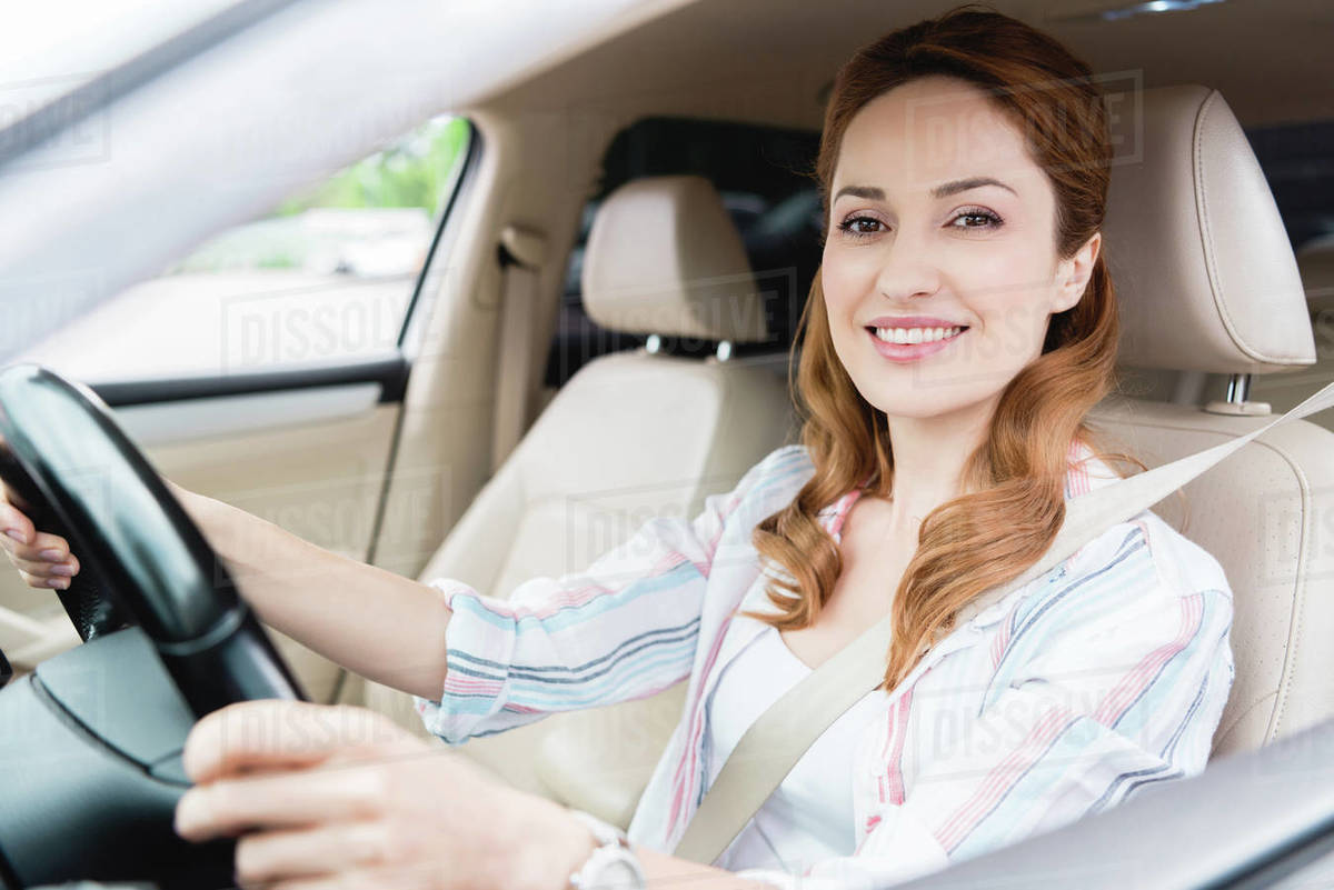 Side view of smiling woman looking at camera while driving car ...