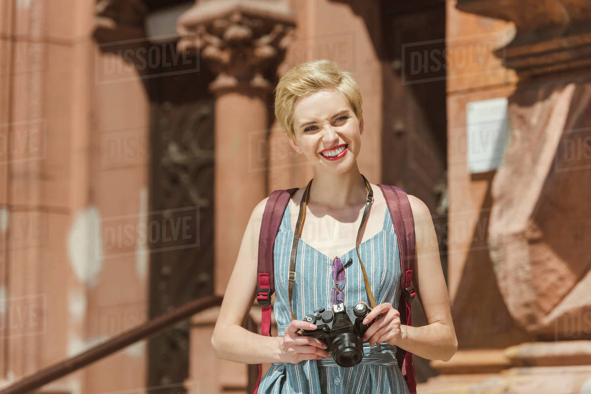 Smiling traveler with backpack and photo camera in city - Stock Photo ...