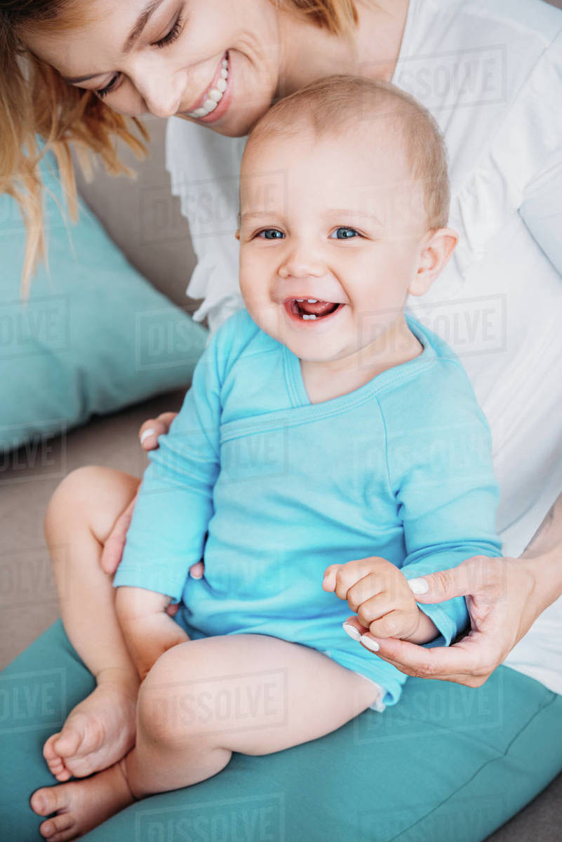 Close-up portrait of laughing little child sitting on knees of mother ...