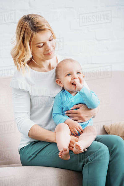 Mother holding her adorable child on knees while sitting on couch ...