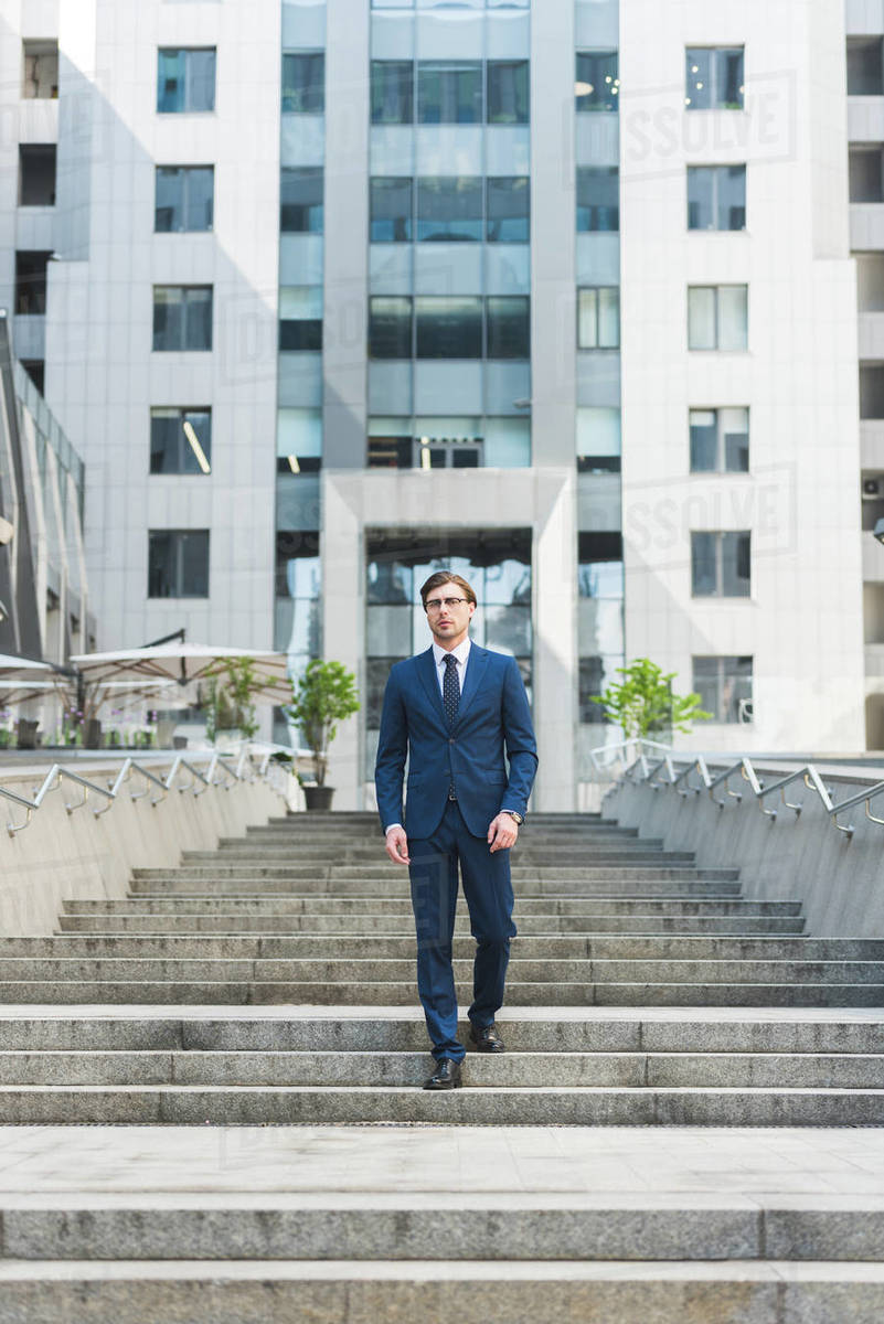 Stylish young businessman walking down stairs in business district ...