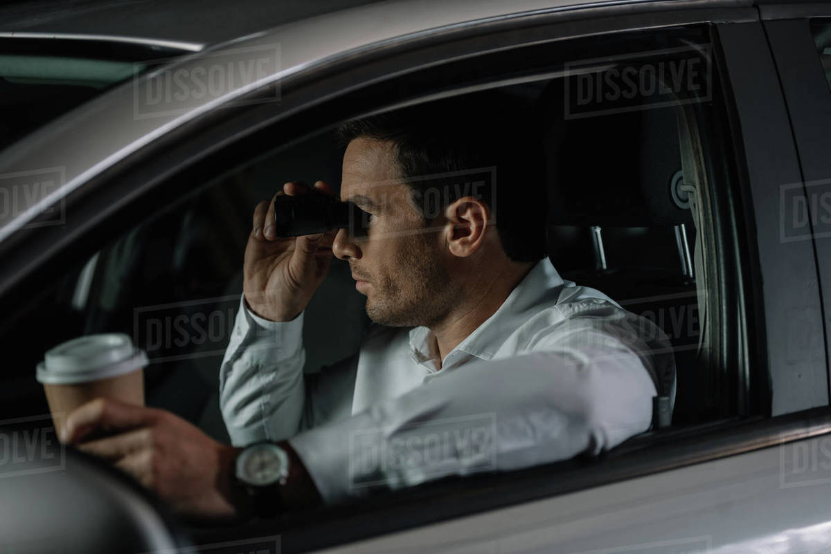 Side view of undercover male agent doing surveillance by binoculars and ...