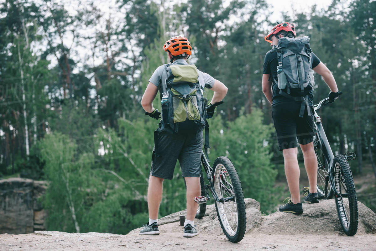Rear view of male extreme cyclists in protective helmets standing with ...
