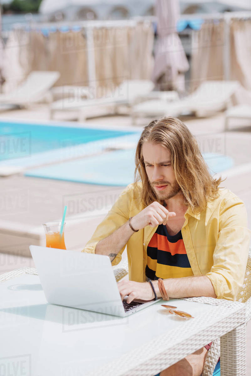 Handsome young man drinking cocktail while sitting near pool - Stock ...