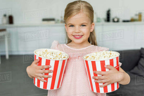 Adorable little child holding boxes with popcorn and smiling at camera ...