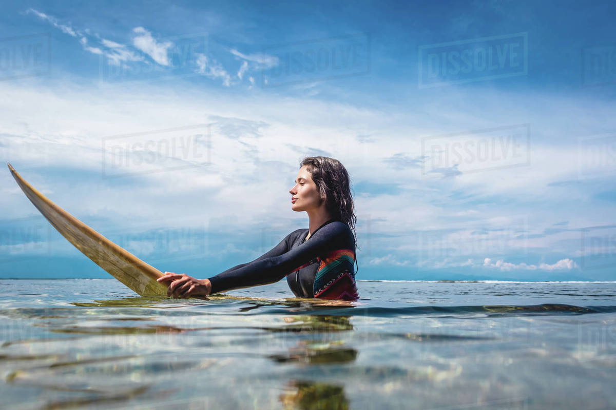 Side view of young sportswoman in wetsuit on surfing board in ocean at ...
