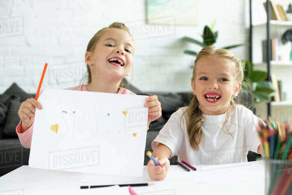Portrait of cheerful kids with drawing at table with pencils at home ...
