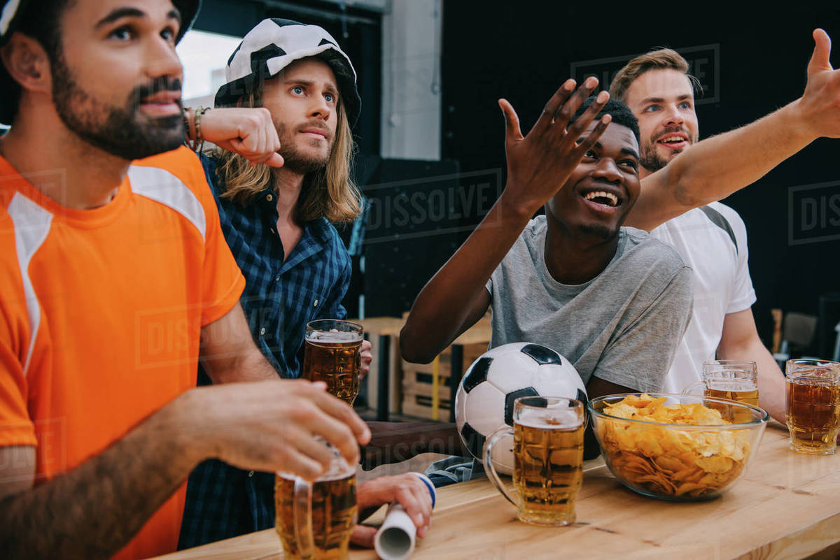 Smiling multicultural group of male football fans gesturing by hands ...