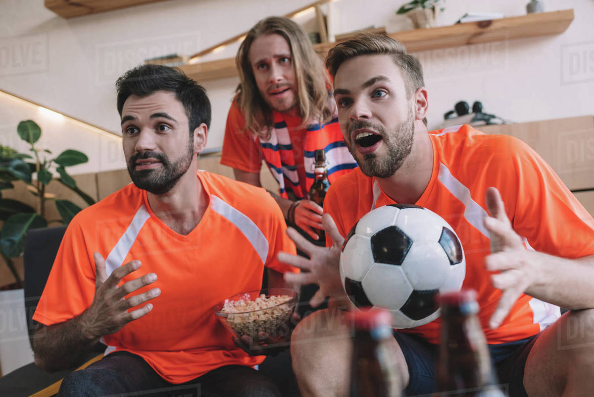 Emotional young male football fans in orange t-shirts with ball and ...
