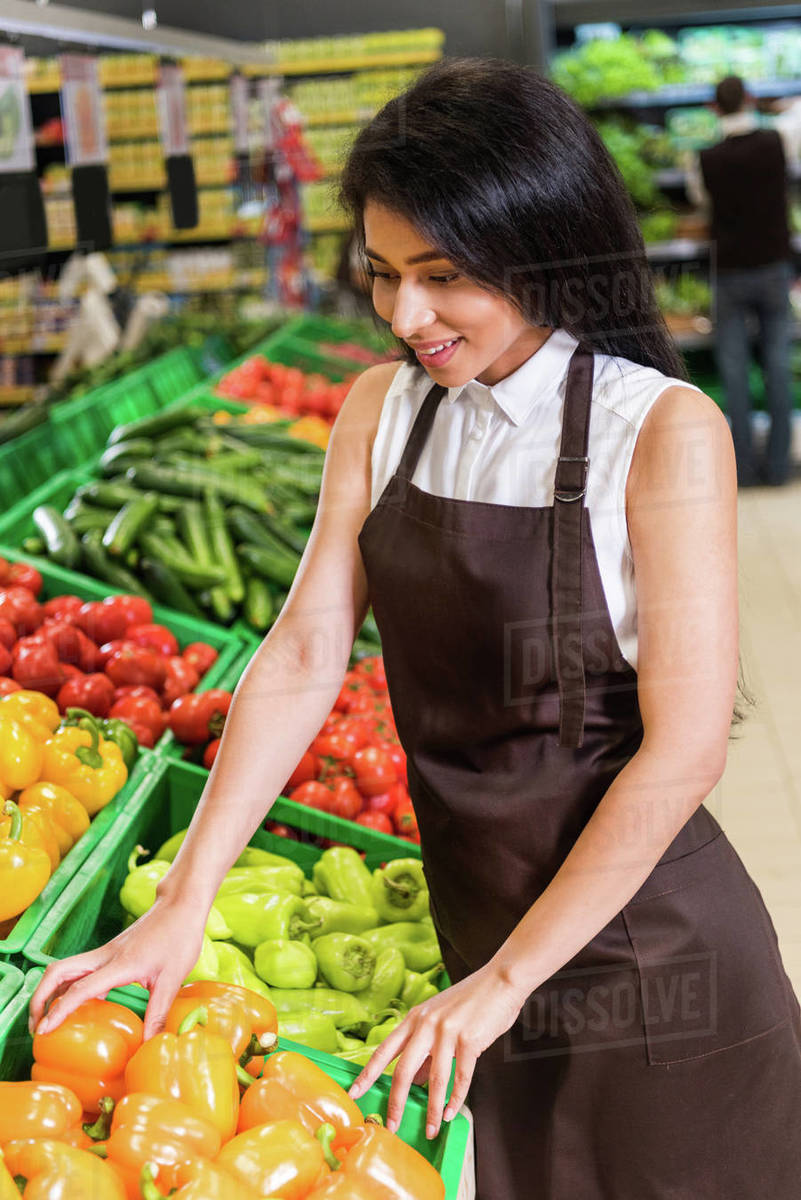 Smiling african american female shop assistant in apron arranging bell ...