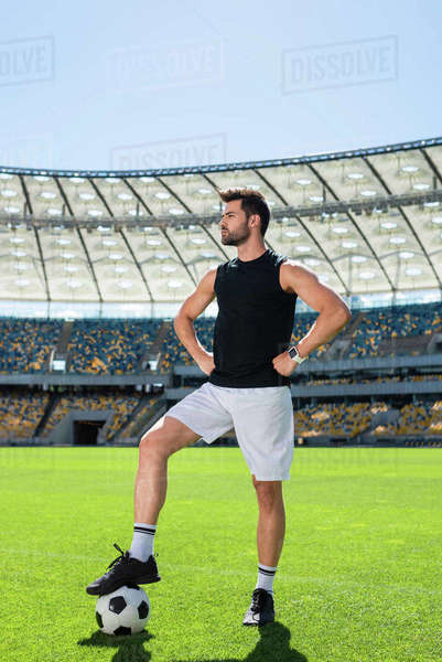 Serious young soccer player standing at sports stadium with ball and ...