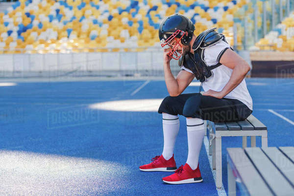 Side view of young american football player holding cage of helmet ...