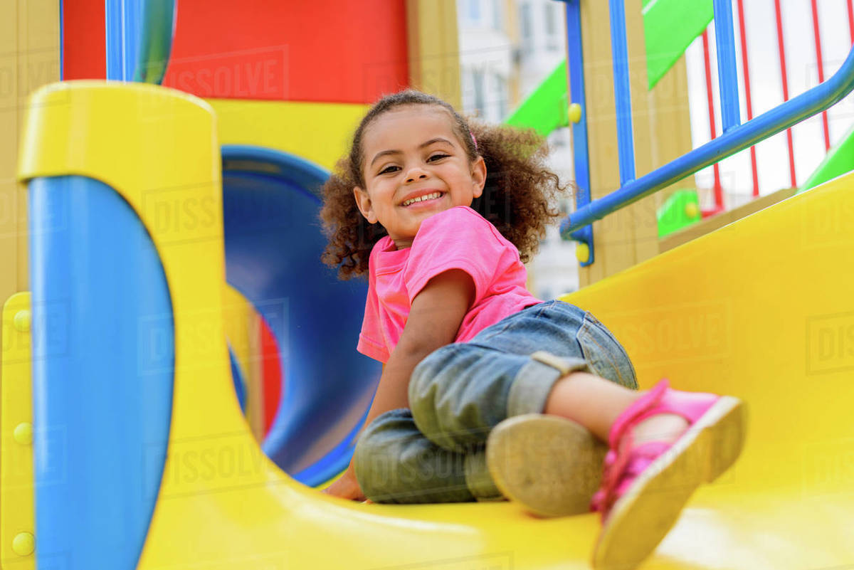 Happy african american little kid sliding down from hill at playground ...