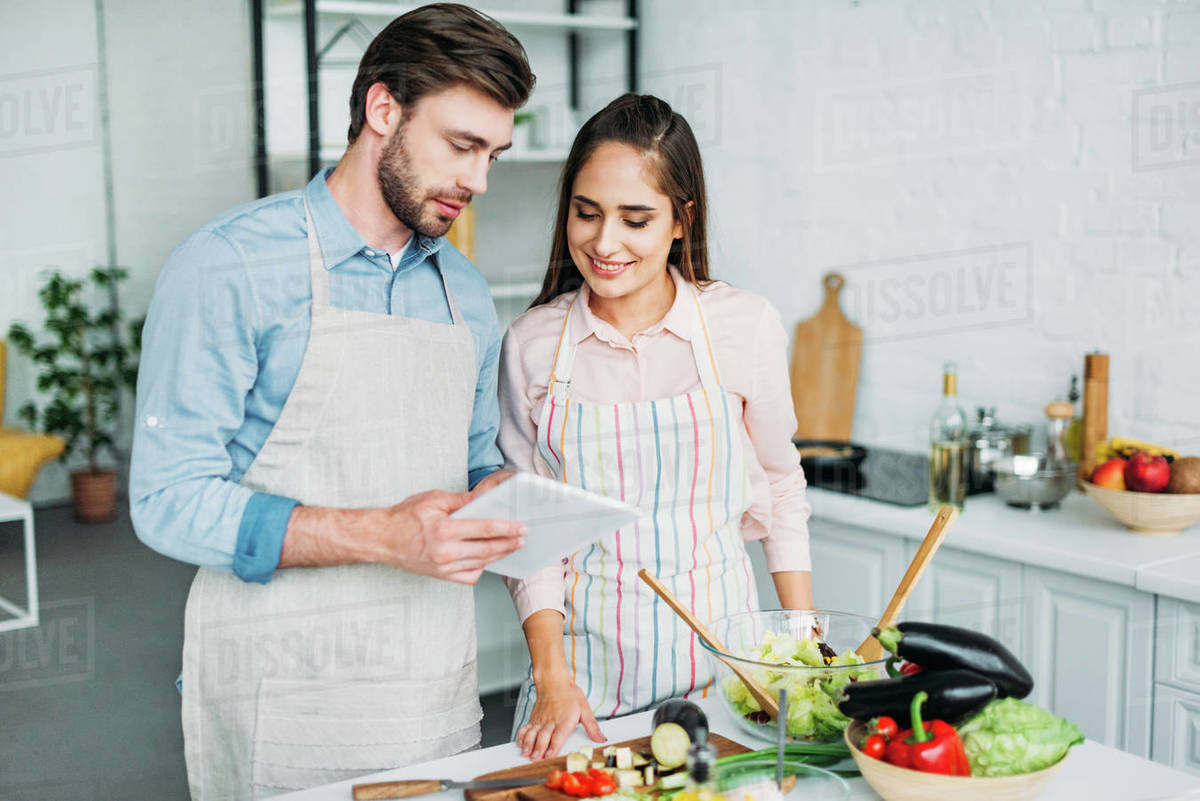 Couple looking at tablet with recipe while cooking in kitchen - Stock ...