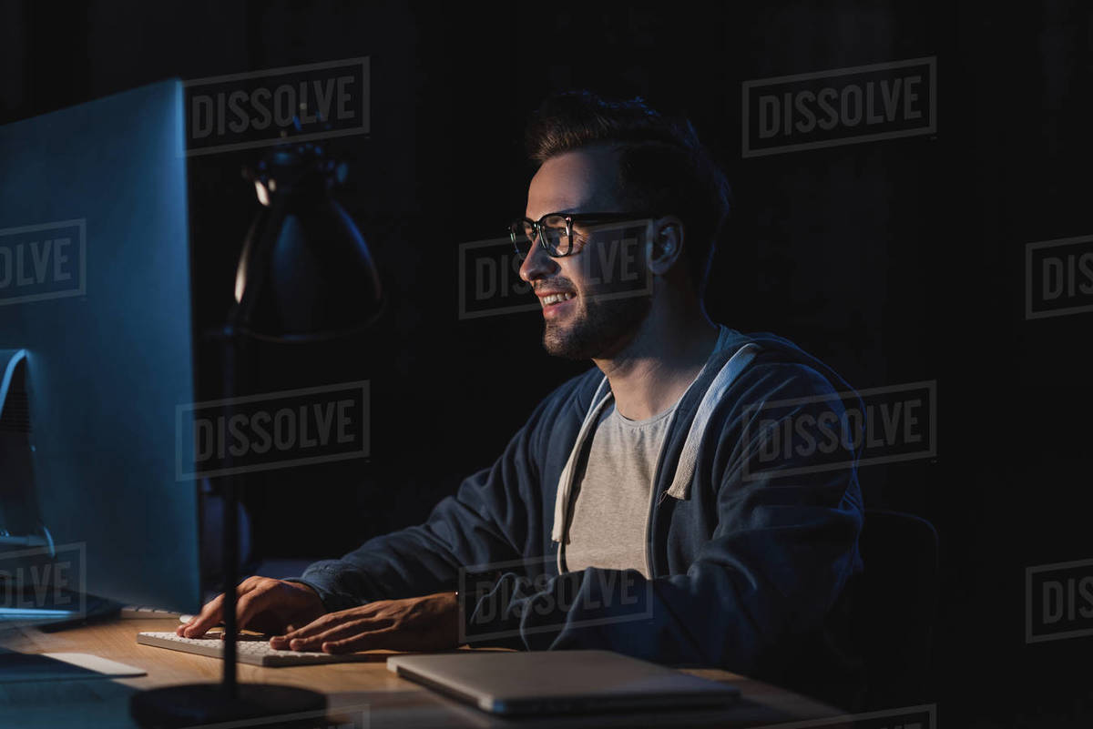 smiling young programmer in eyeglasses working with desktop computer at night - Stock Photo ...