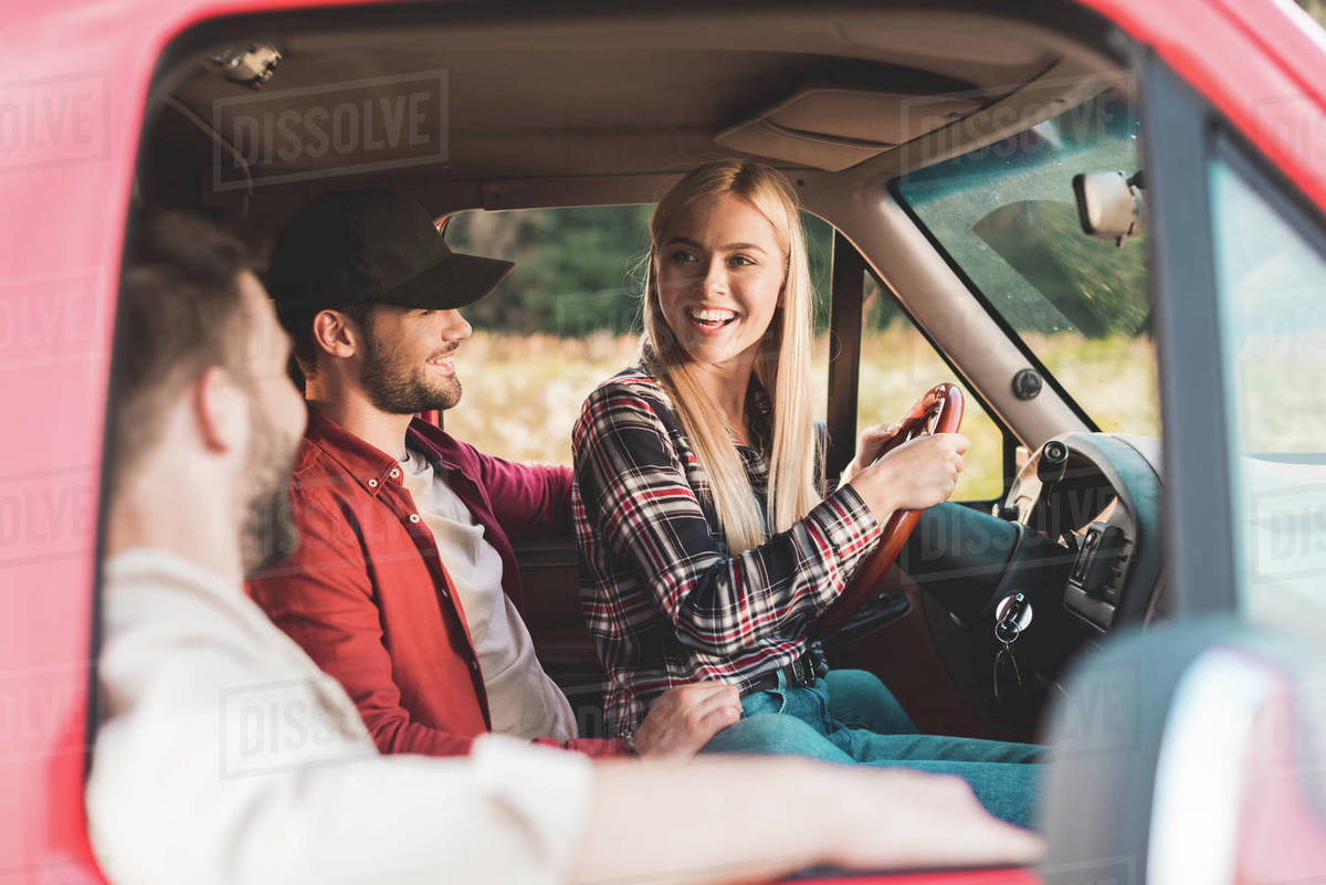group of happy friends travelling by car and riding by flower field ...