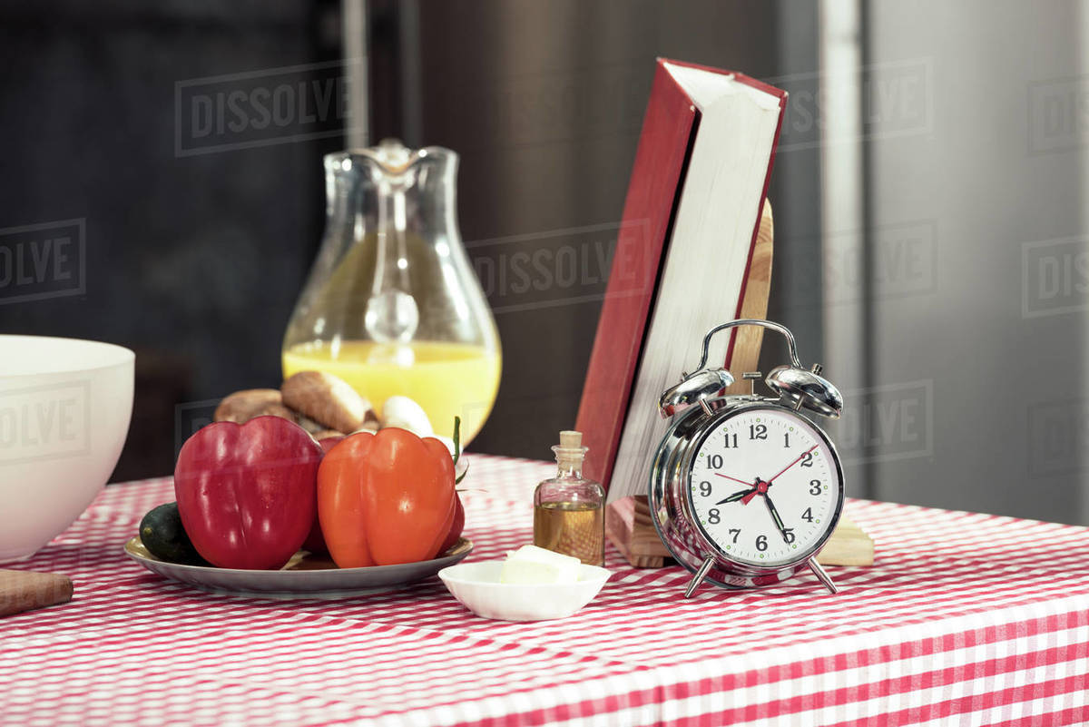 vintage alarm clock with various products and recipe book on table ...