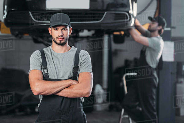 Professional mechanic in overalls with crossed arms, while colleague ...