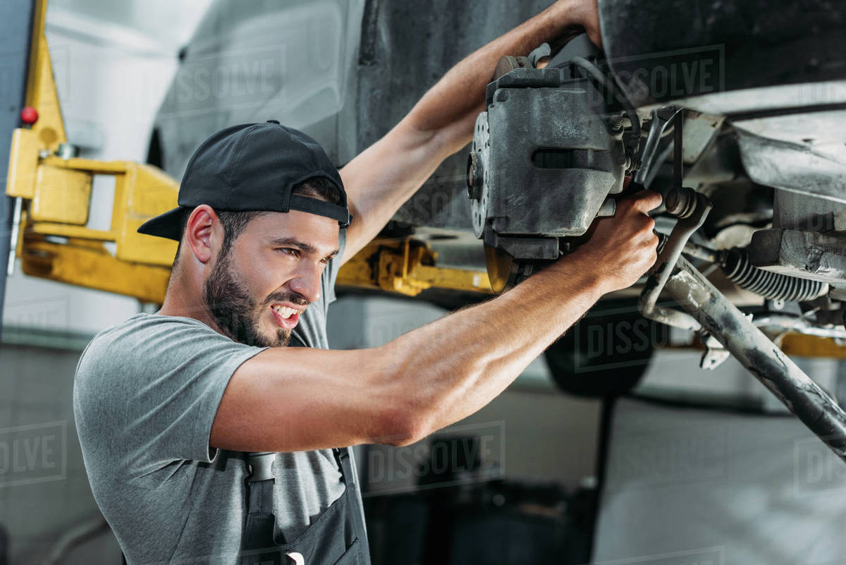 Engineer in overalls repairing car in mechanic shop - Royalty-free ...