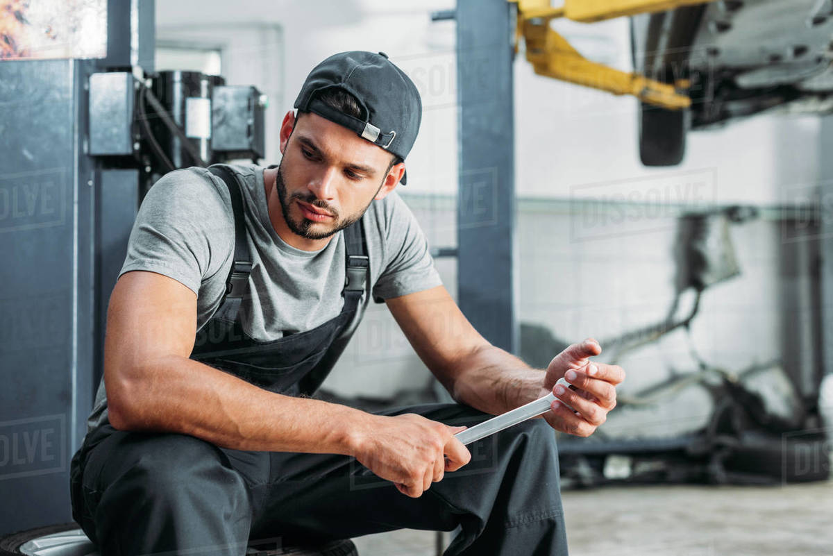 Professional workman holding wrench and sitting in mechanic shop ...