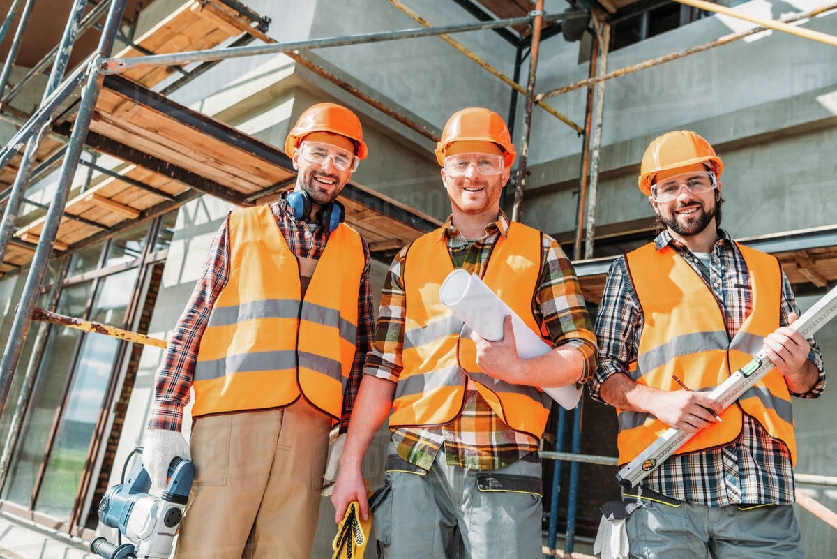 Bottom view of group of happy equipped builders looking at camera at ...