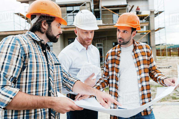 Group of architects with building plan having conversation in front of ...