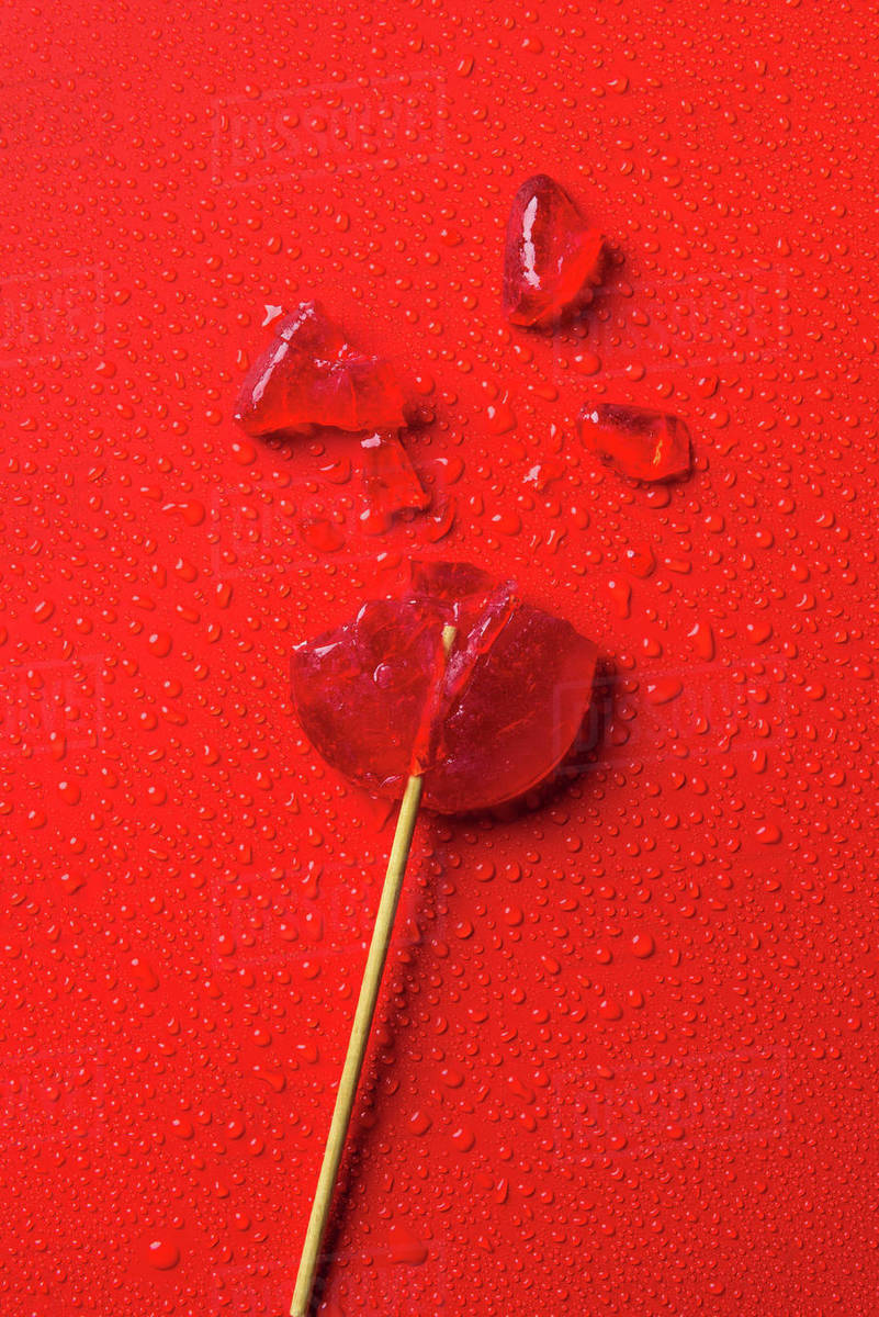 top view of broken lollipop on red surface with water drops - Stock ...